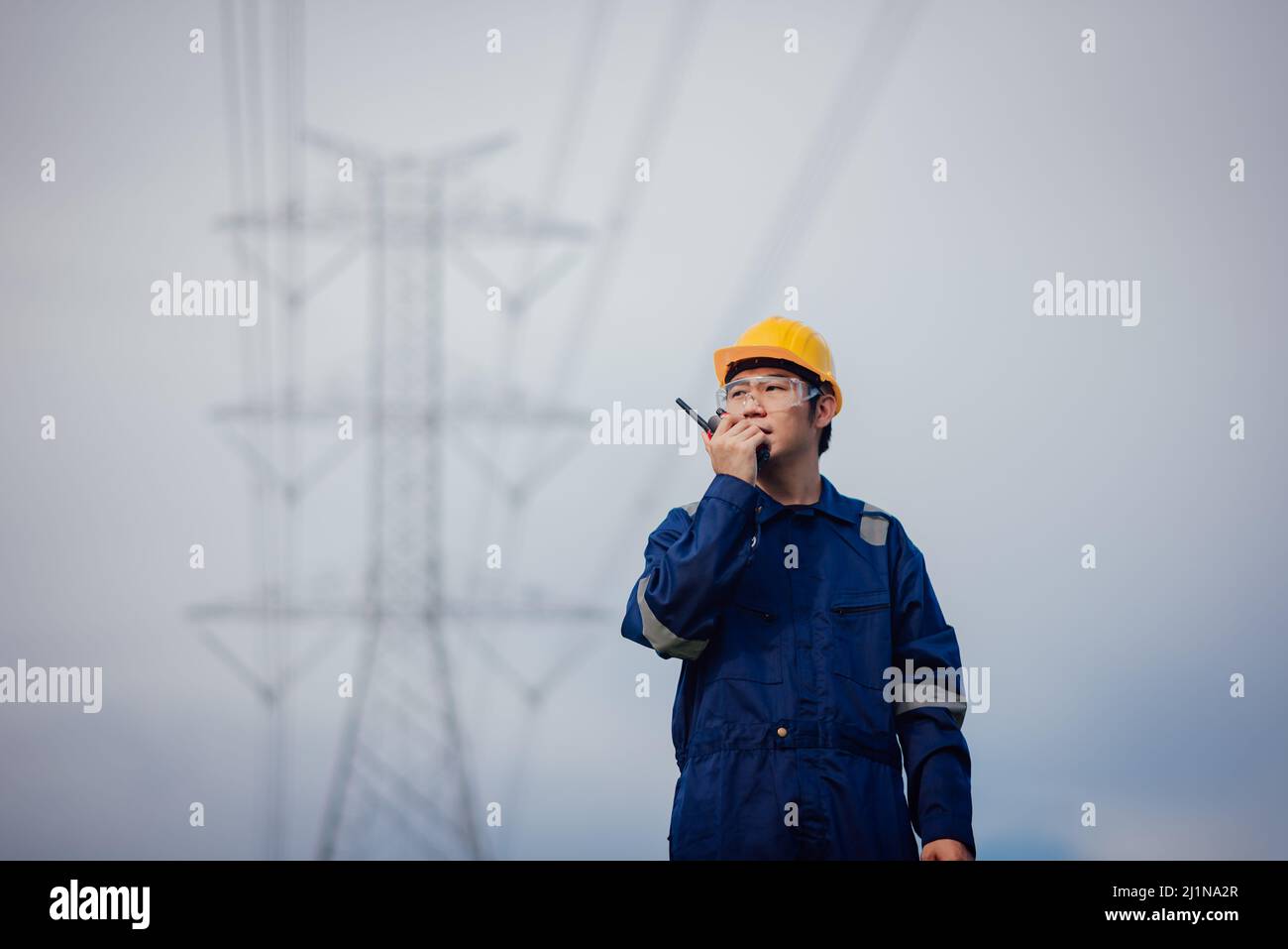 A male power engineer in a yellow helmet inspects the power line under ...
