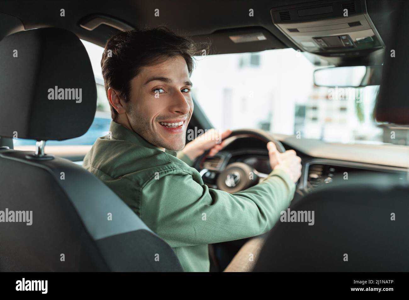 Handsome young man looking back at camera, sitting in car, parking auto ...