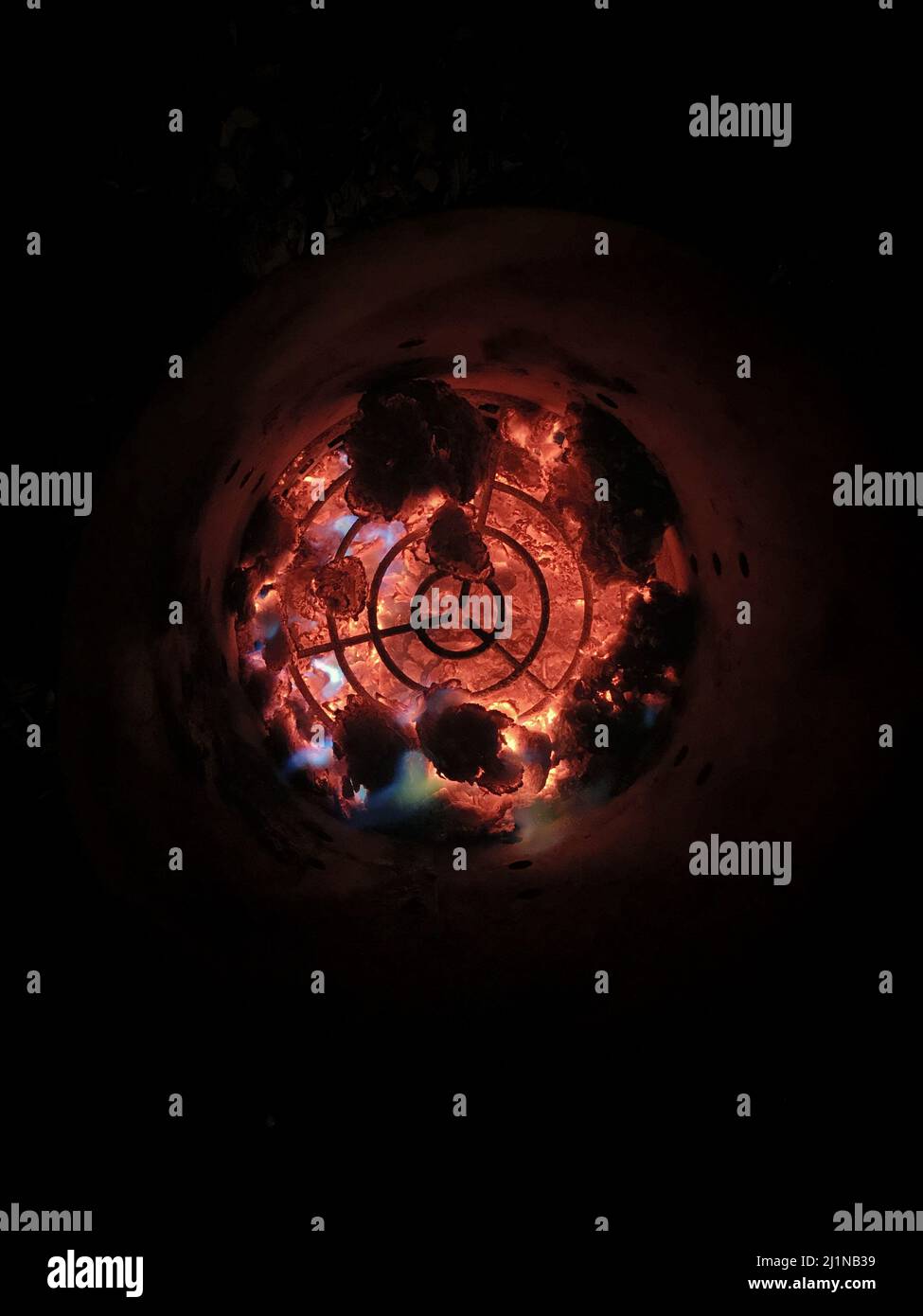 A top view of a grill fire pit with coals and blue flames coming off it ...