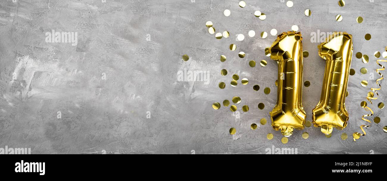 Yellow foil balloon number, number eleven on a concrete background ...