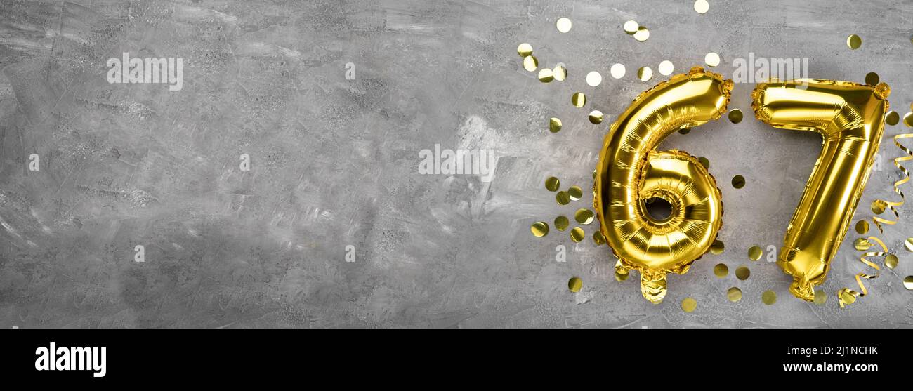 Yellow foil balloon number, number sixty-seven on a concrete background ...