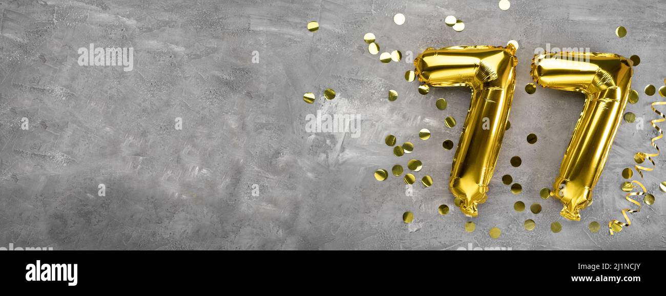 Yellow foil balloon number, number seventy seven on a concrete ...