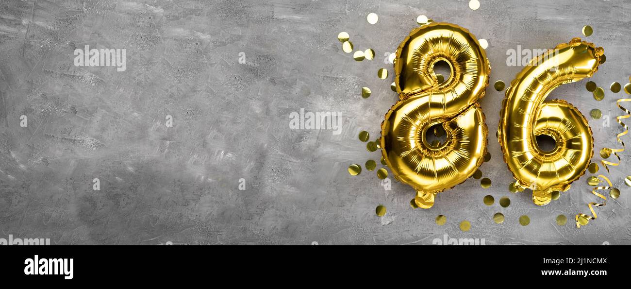 Yellow foil balloon number, number eighty six on a concrete background ...