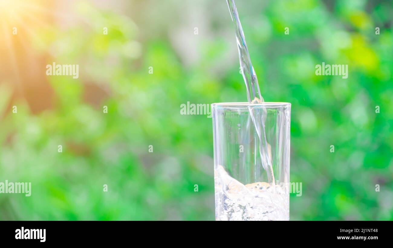 The pure water from jug into glass on wooden table on nature background ...