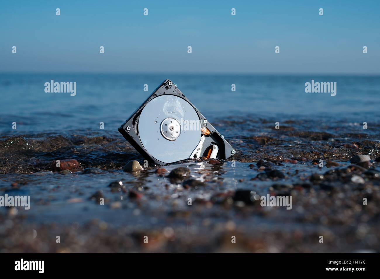 a computer hard disk lies in the shore sand of the sea and is washed by ...