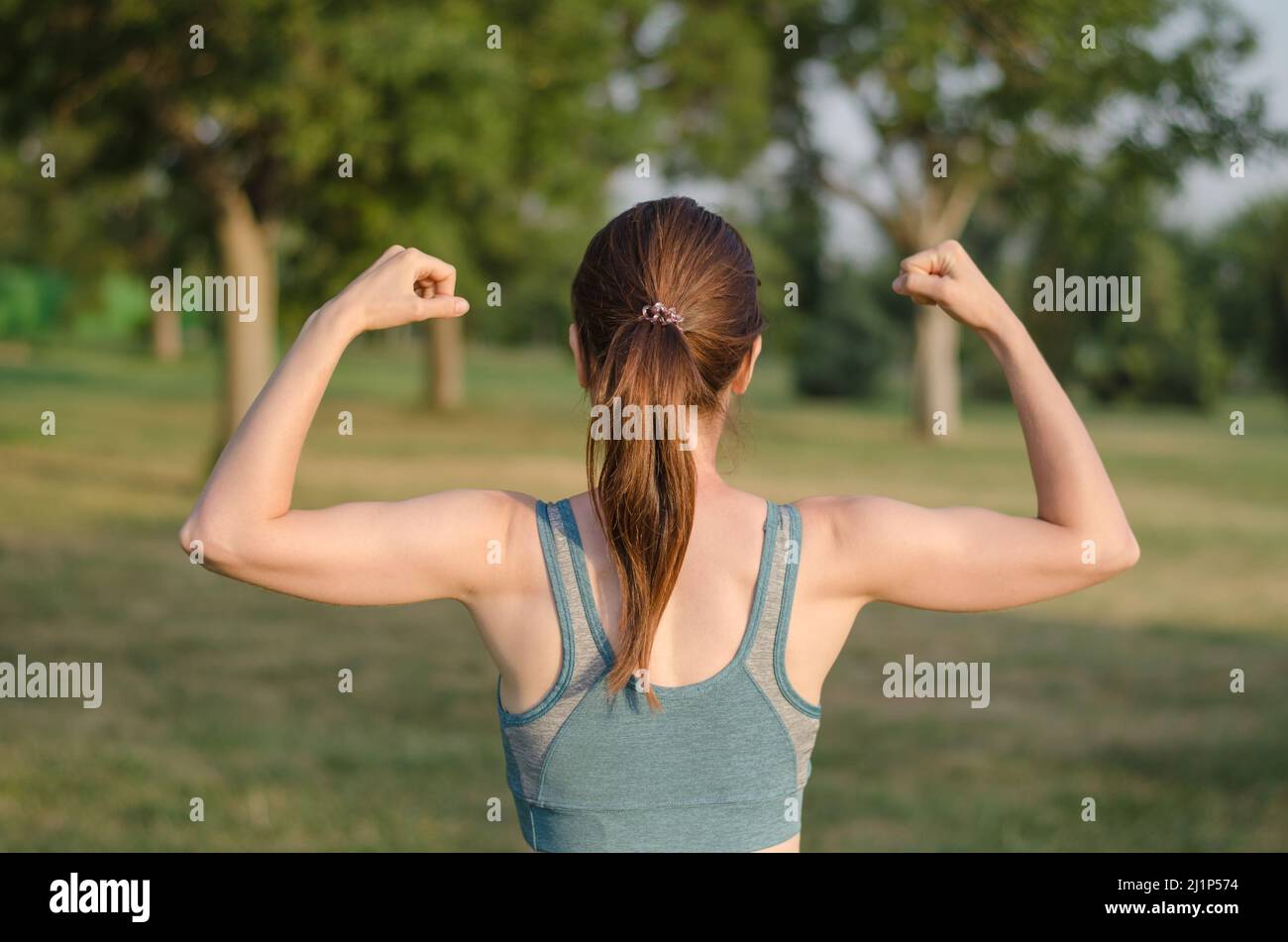 Woman athlete demonstrates her arm muscles in nature. Rear view of ...