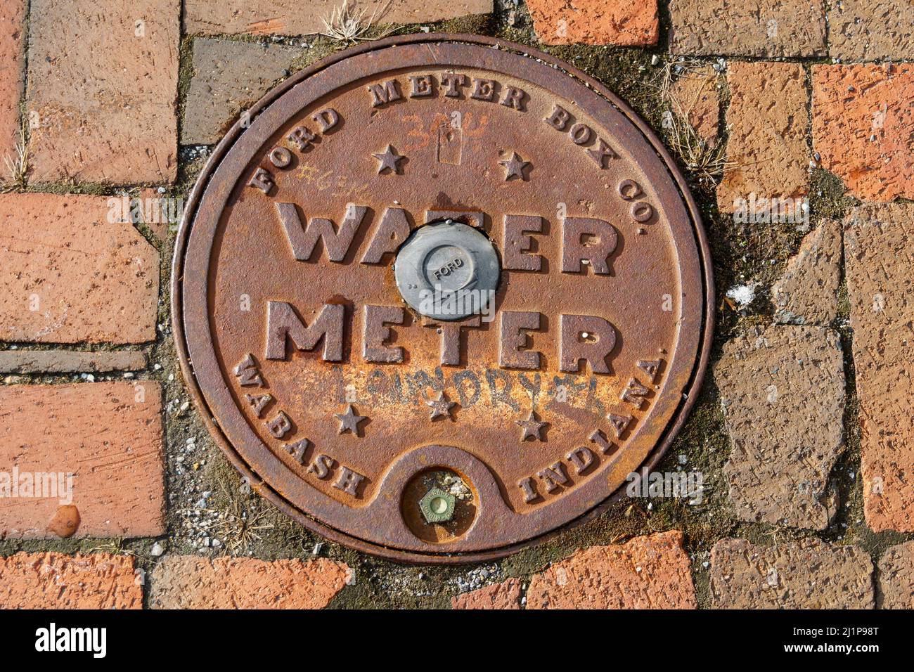 Rusted water meter access hatch on a brick street. Ford meter box ...