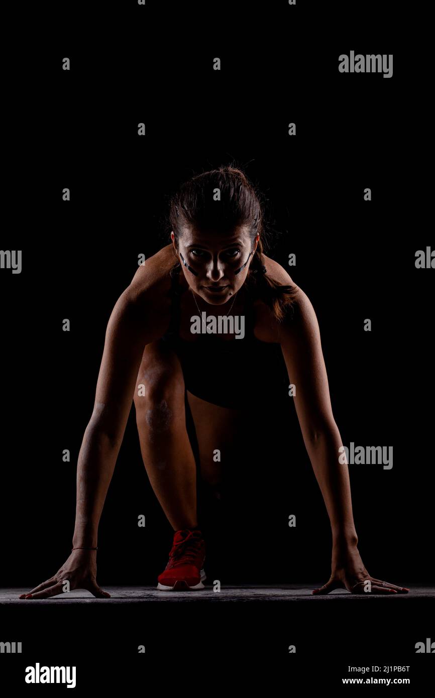 Side lit silhouette fit girl in race start position against dark ...