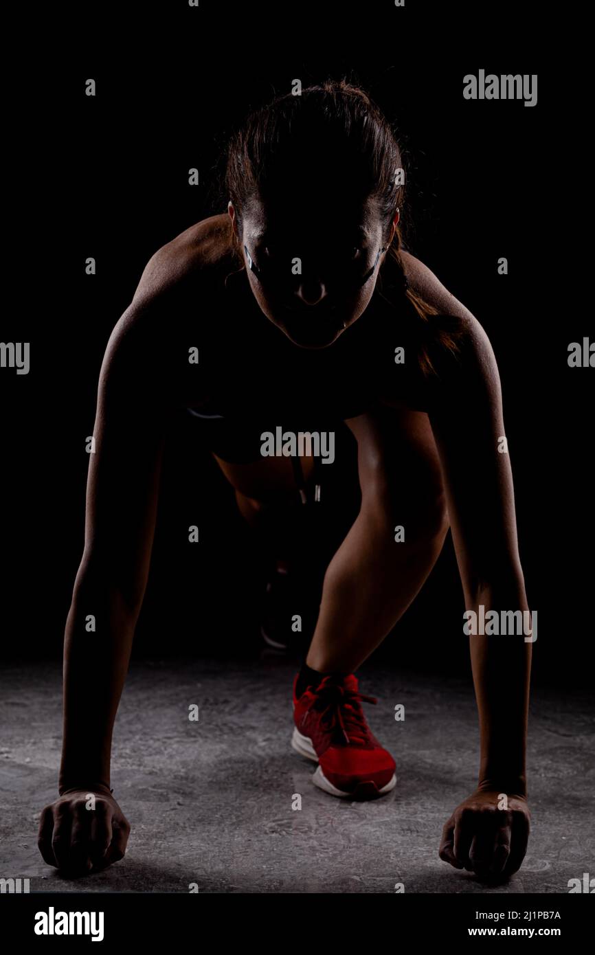 Side lit silhouette fit girl in race start position against dark ...