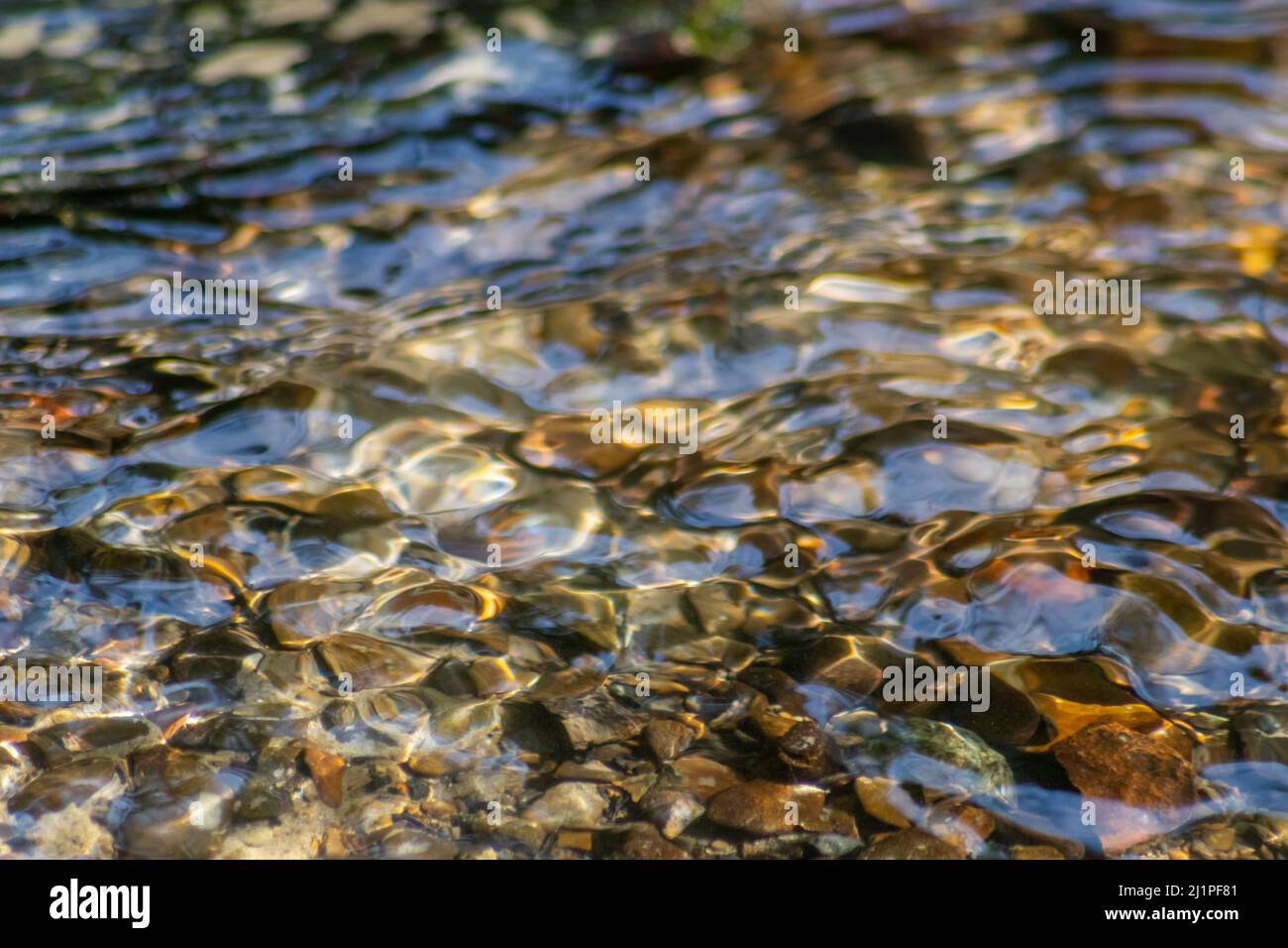 Stones in sparkling water with sunny reflections in water of crystal ...