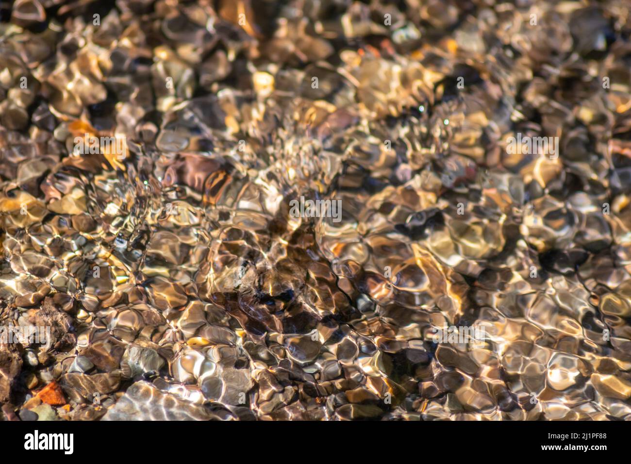 Stones in sparkling water with sunny reflections in water of crystal ...