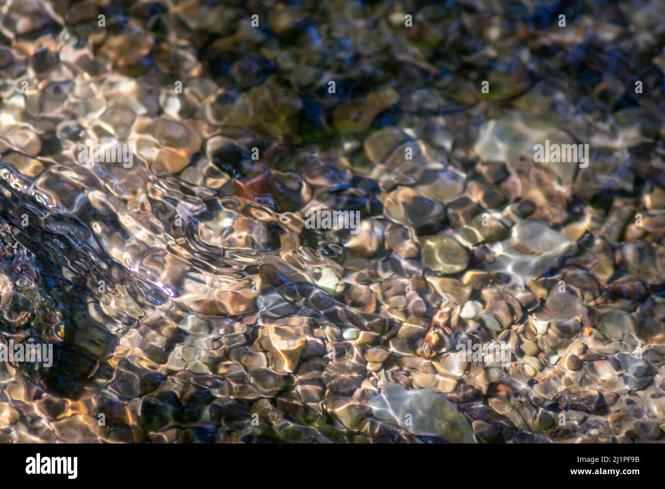 Stones in sparkling water with sunny reflections in water of crystal ...