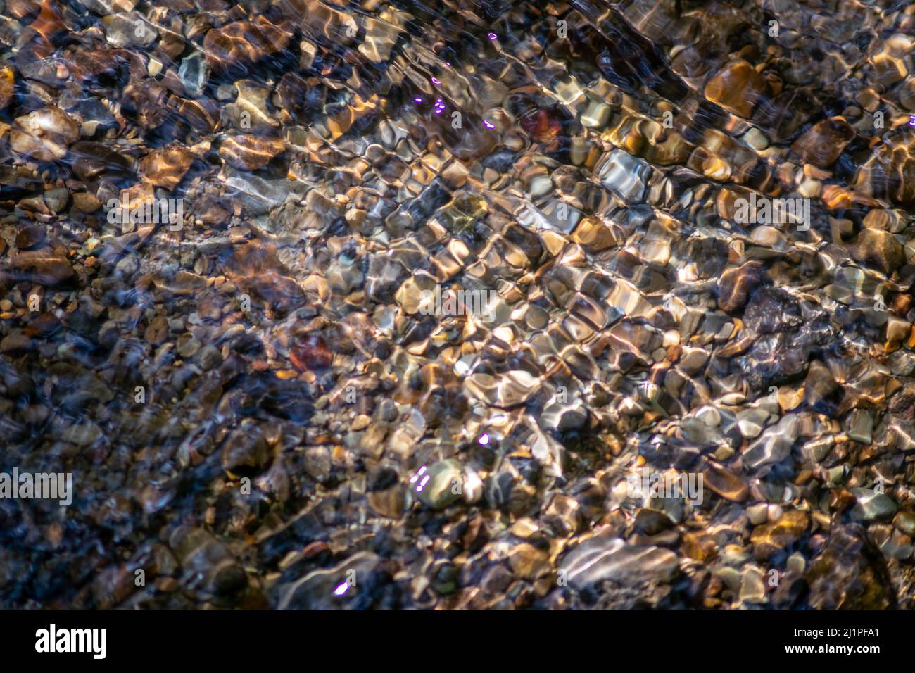 Stones in sparkling water with sunny reflections in water of crystal ...