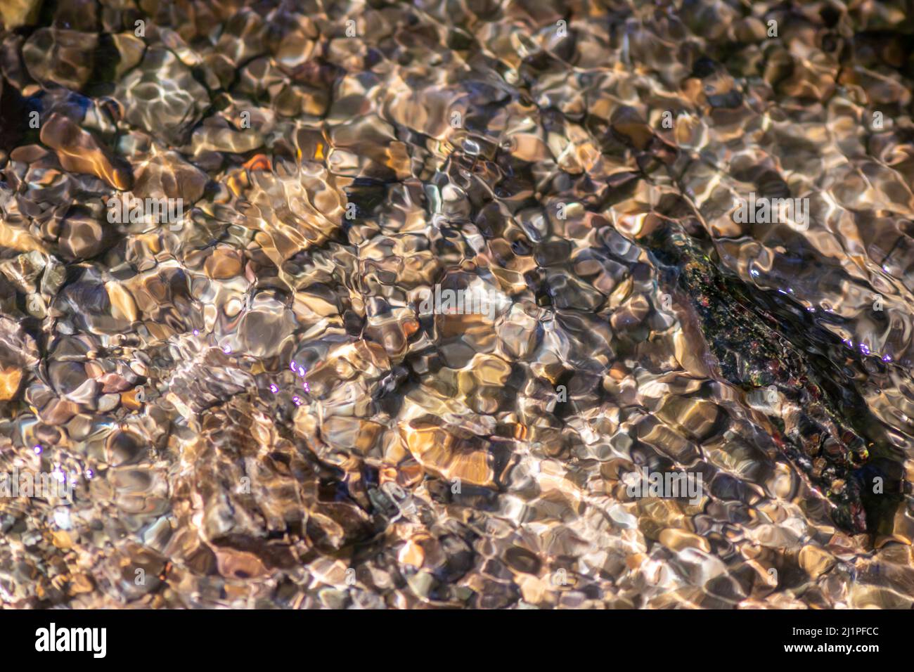 Stones in sparkling water with sunny reflections in water of crystal ...