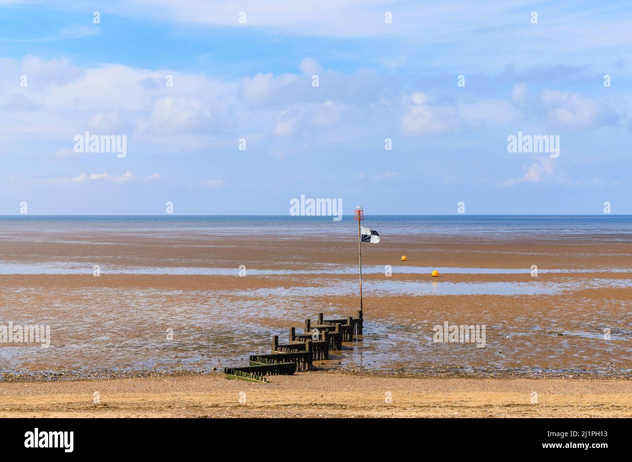 Wooden groyne with black and white flag on a deserted beach at low tide ...