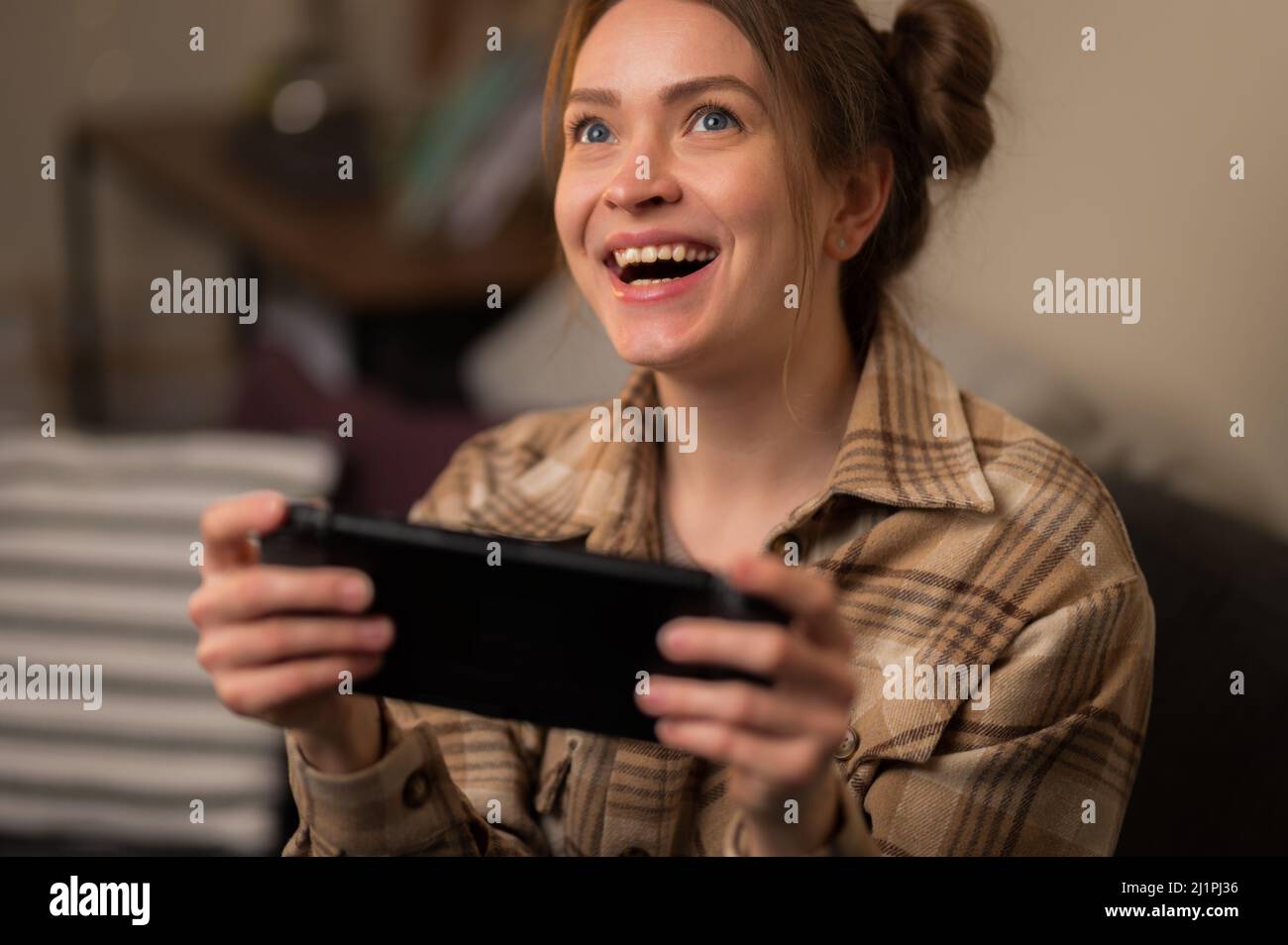 Joyful female gamer plays a video game on a portable game console ...