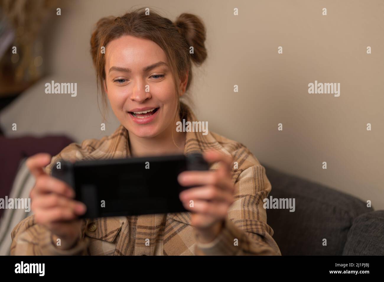 A fair-haired girl gamer has fun playing mobile games on a portable ...