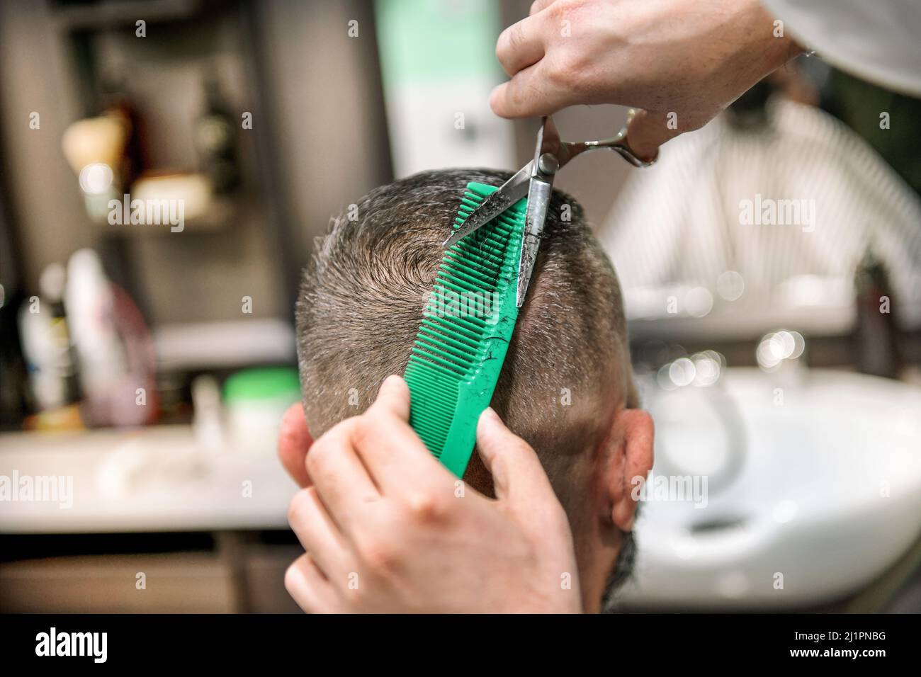 Crop unrecognizable barber with scissors and comb cutting short hair of ...