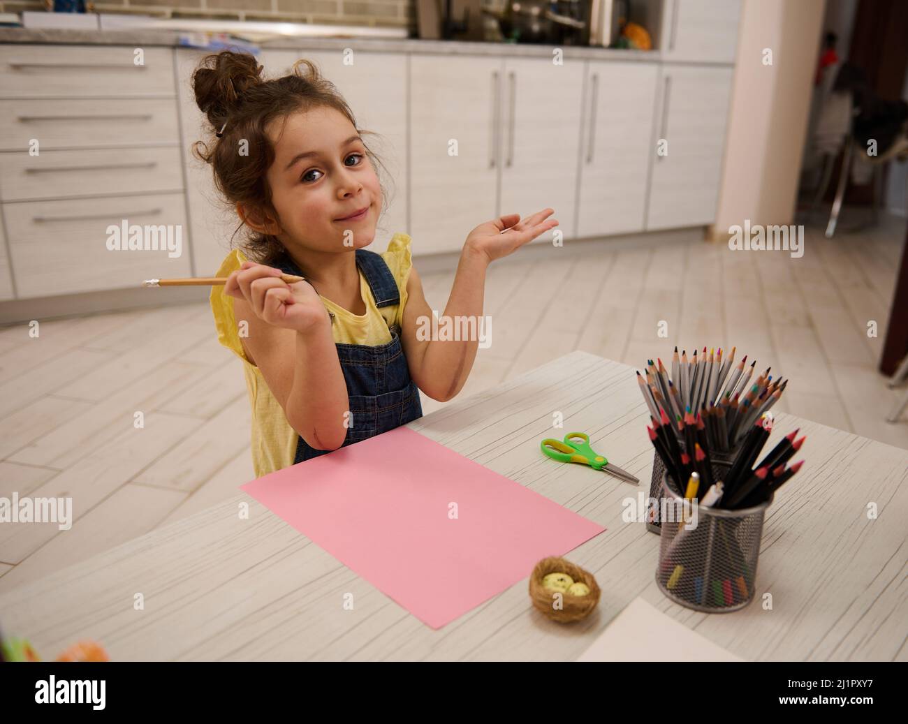 Adorable little Caucasian girl sitting at table with stationery and ...