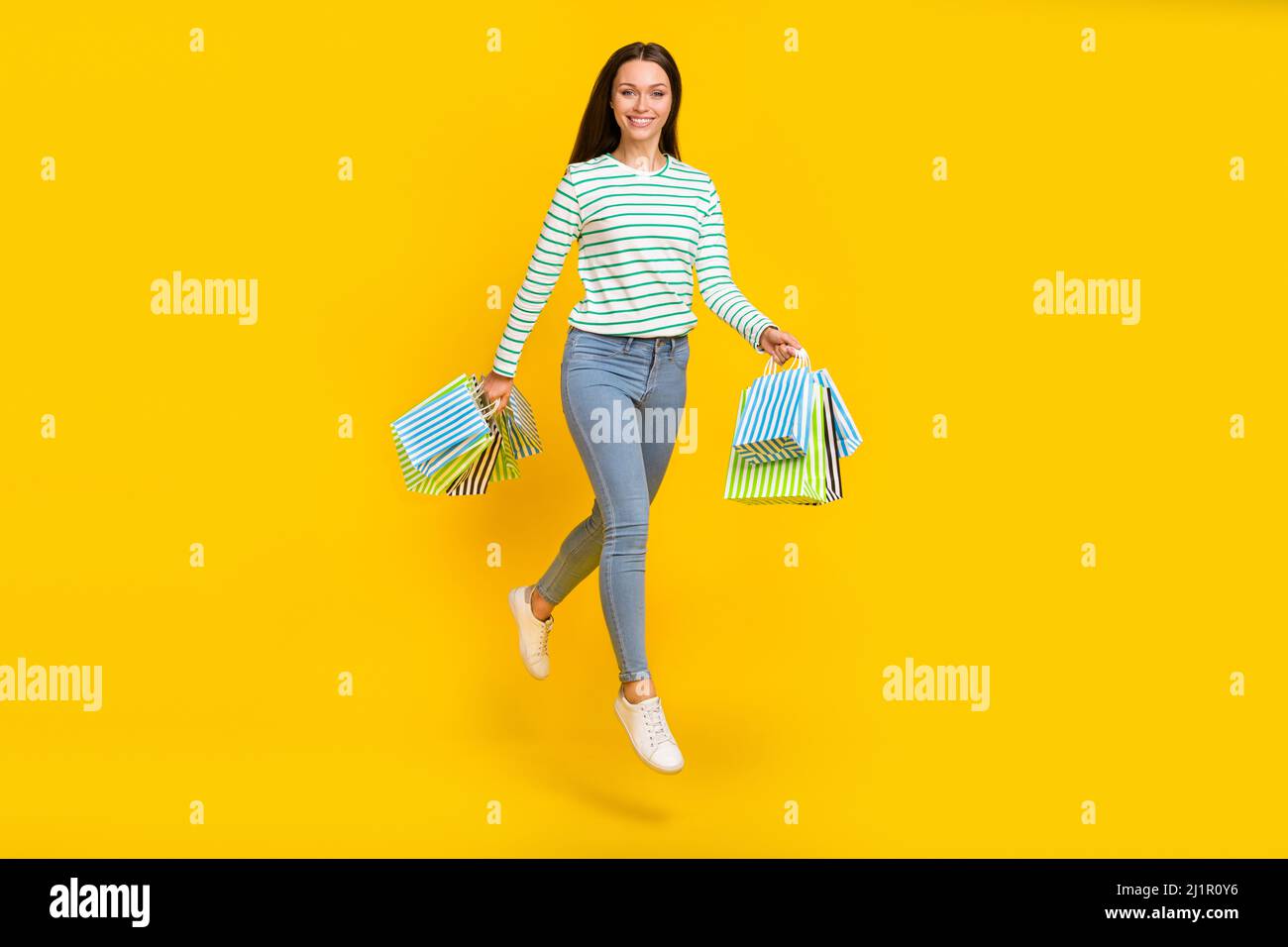 Full size photo of young woman jump walk hold bags shop store deliver ...