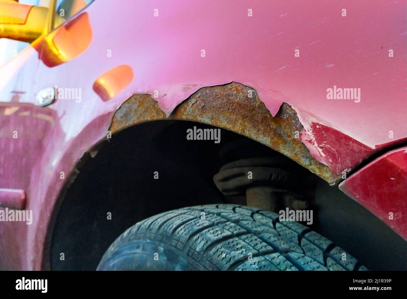 A closeup shot of a red car's rear arch with chipped off and rusty ...