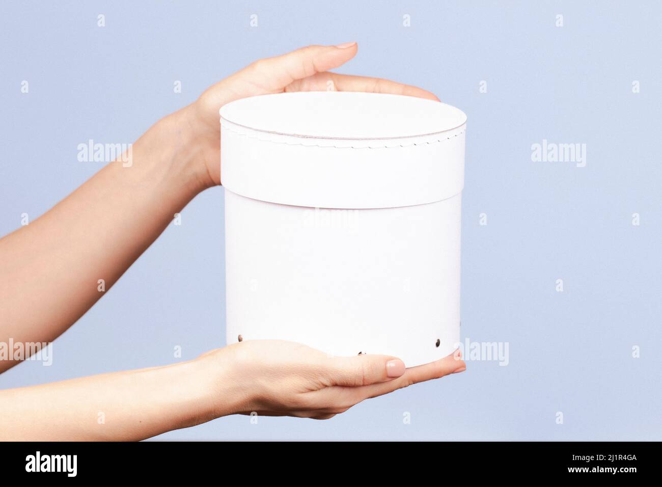 Woman hands holding white round cardboard box with cap on light blue ...