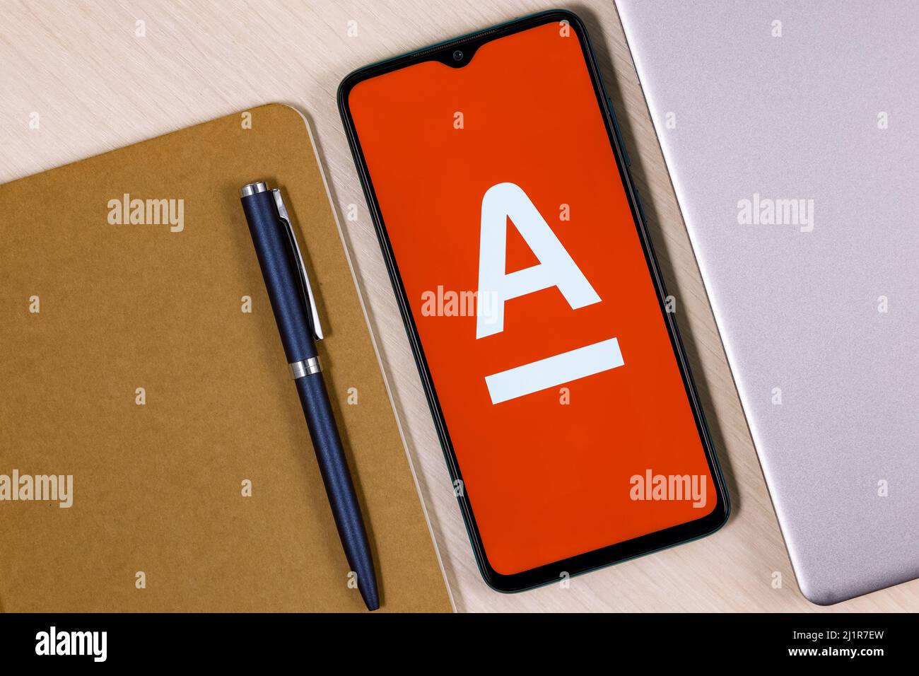 Smartphone with Alfa Bank logo on wooden table next to laptop and ...