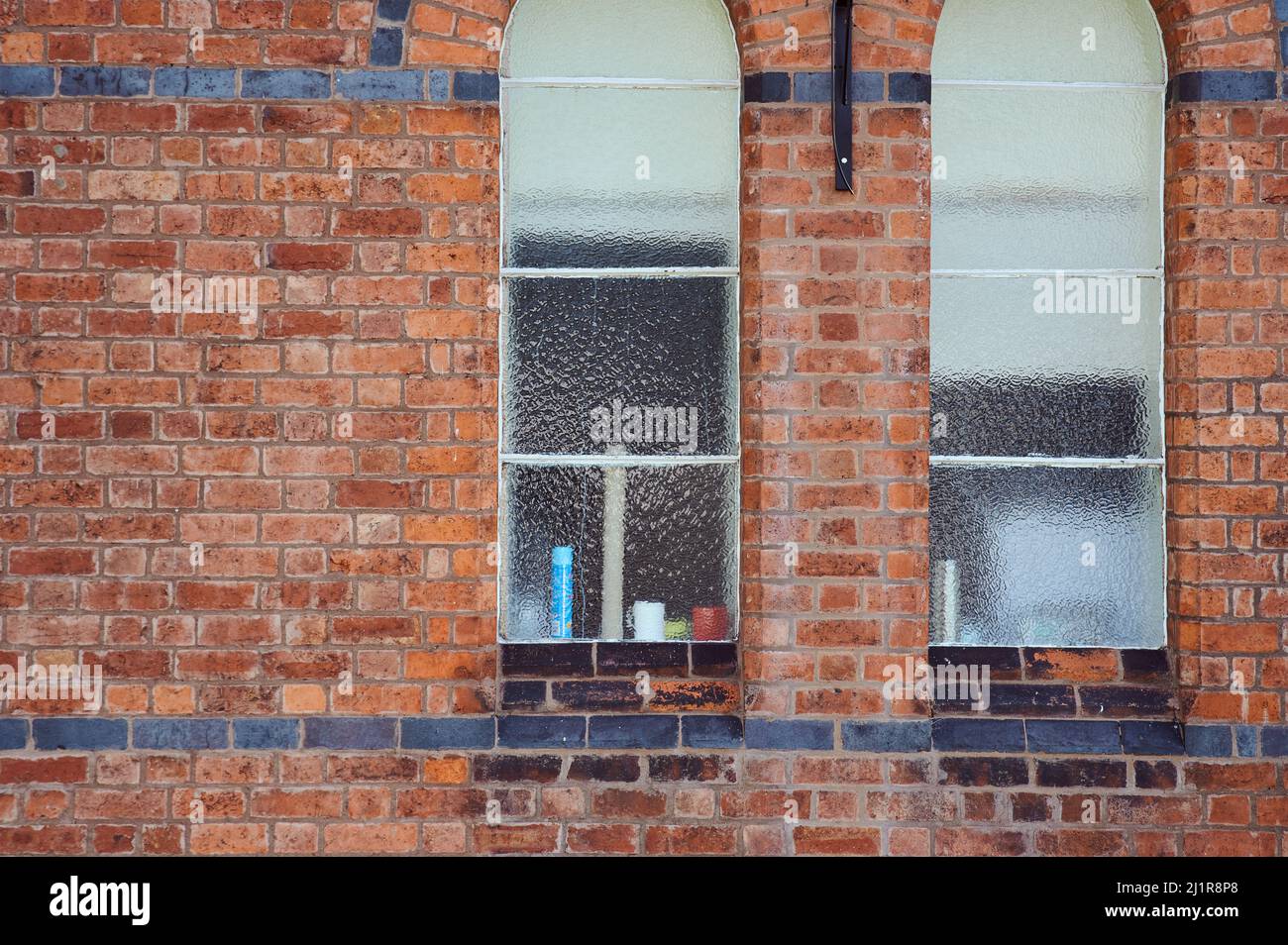 two frosted window on old redbrick wall with line of black bricks and ...