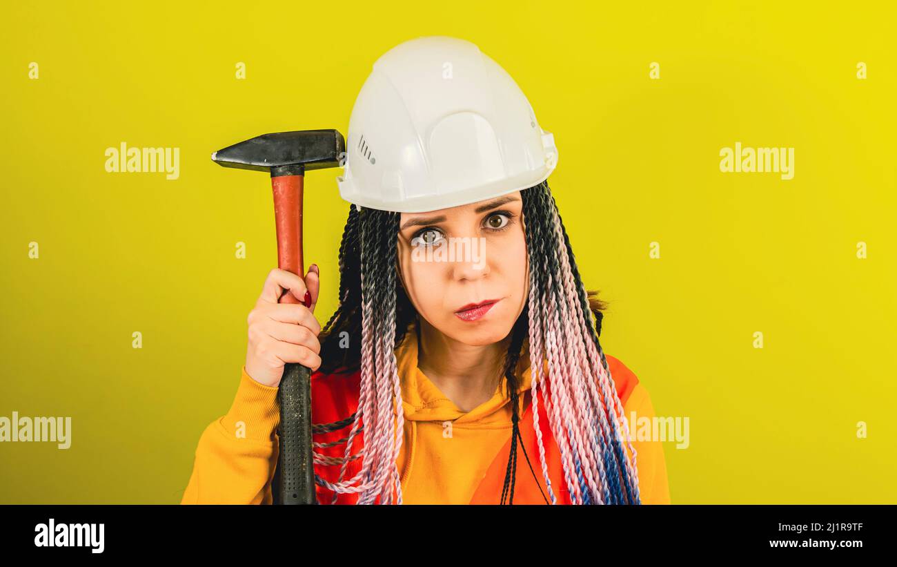 Female construction worker in overalls with hammer on yellow background ...