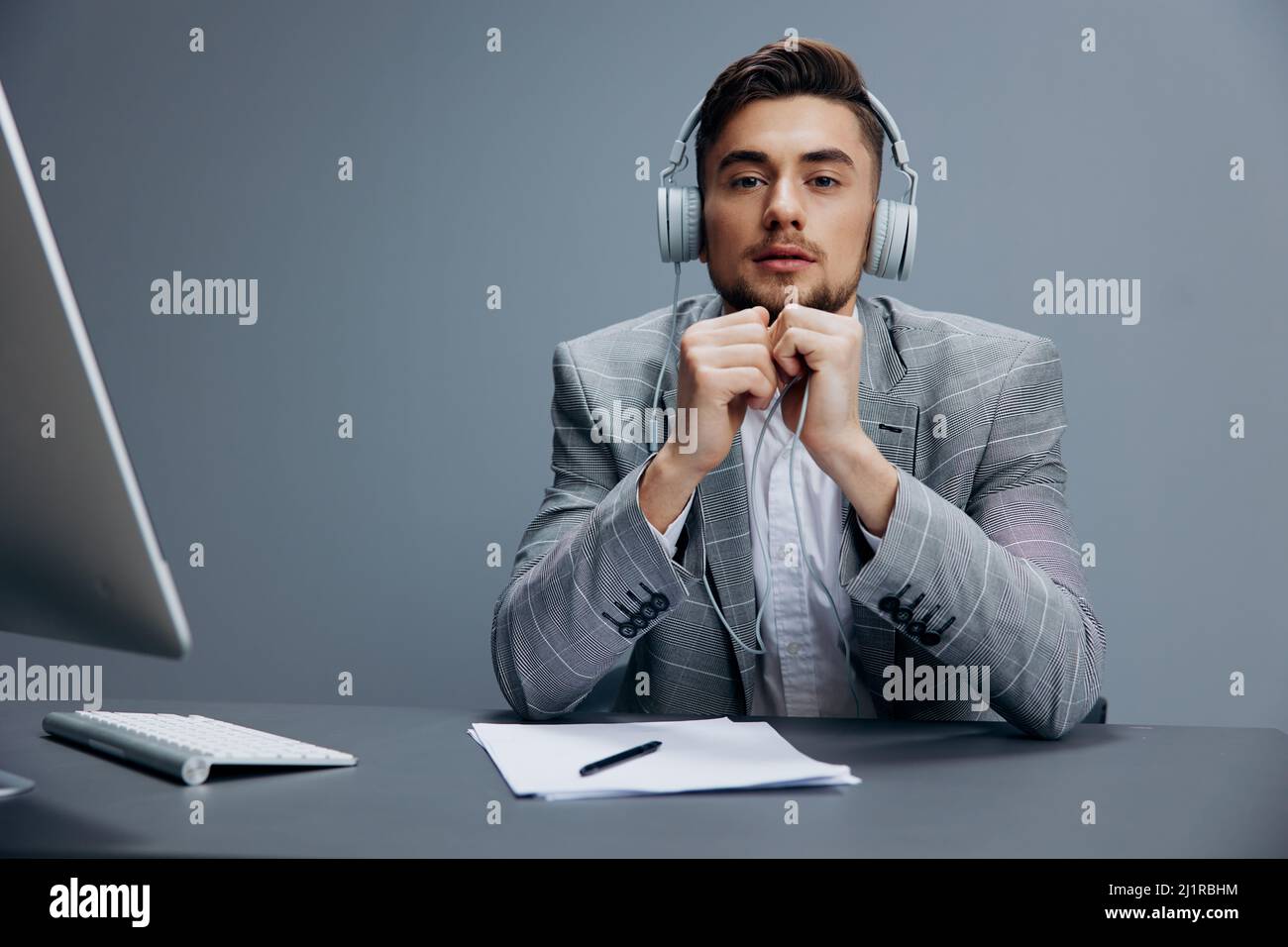 handsome man in headphones in a gray suit sits in front of a computer ...