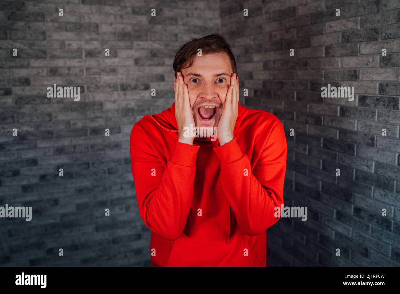 A beautiful emotional man in a red hoodie is happily surprised with ...