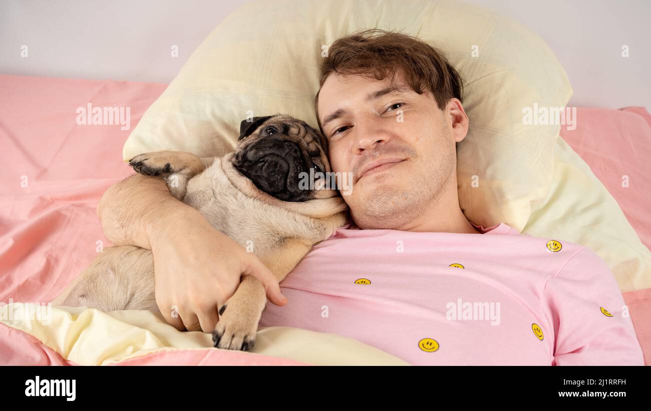 Handsome man lying with dog at bed. Young man in a bed under a rug with ...