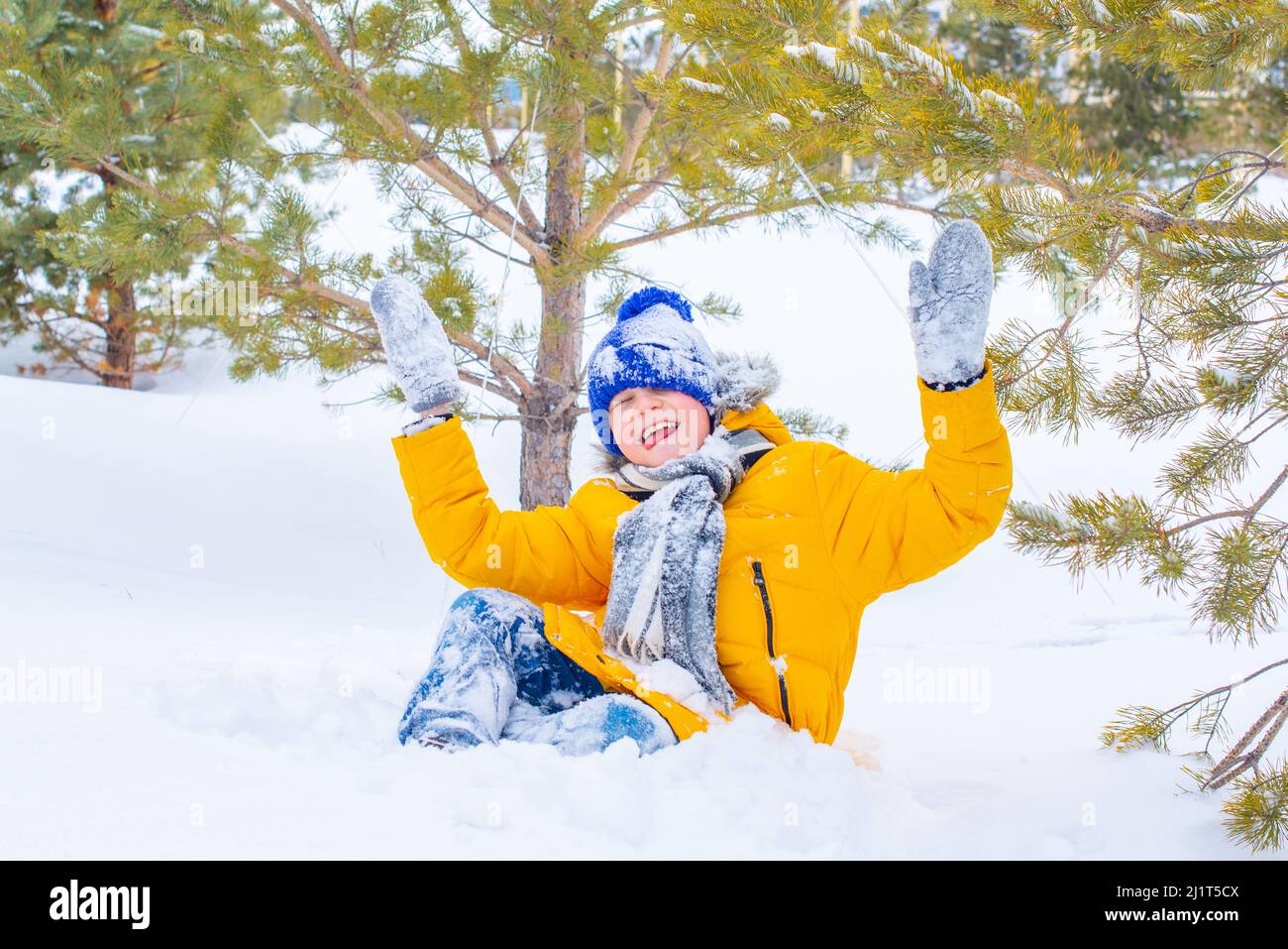 in a very bright yellow jacket and a blue hat, a boy plays in the snow ...