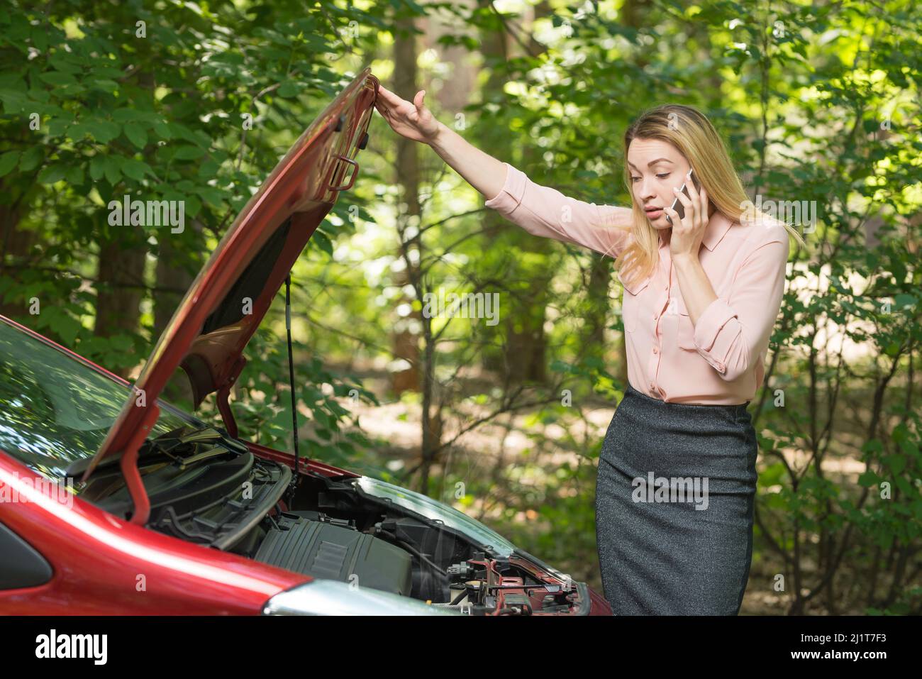 A girl with a broken car that smokes, with a phone, calls for help in a ...