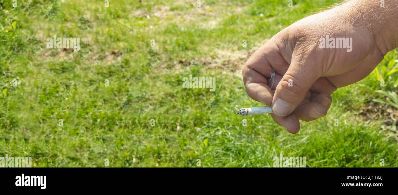 Close-up of a man's hand smoking a cigarette, on a grass background ...