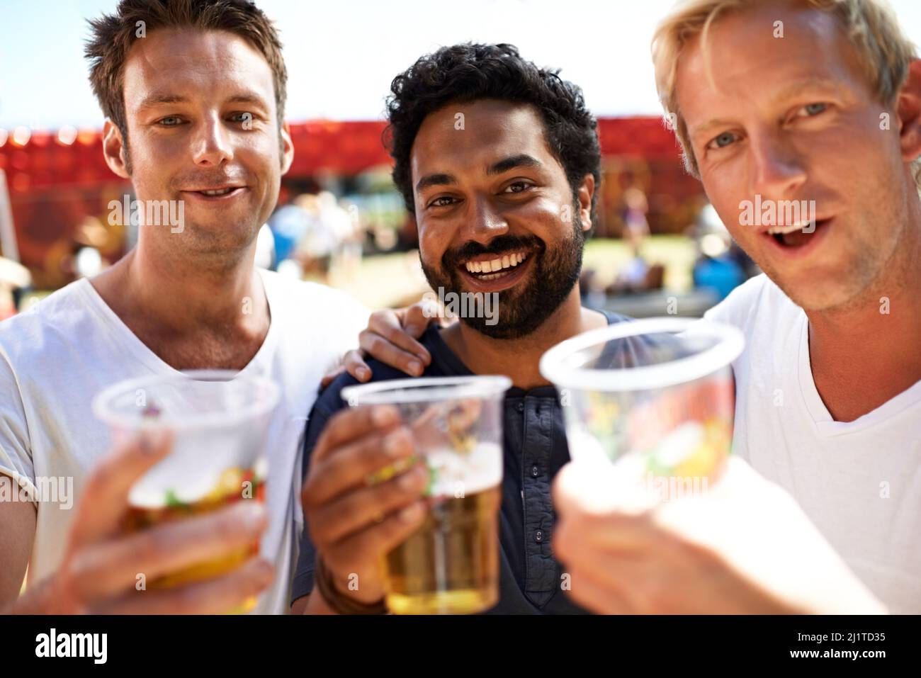 Beer buddies bonding. Three young men toasting their beers at a music ...