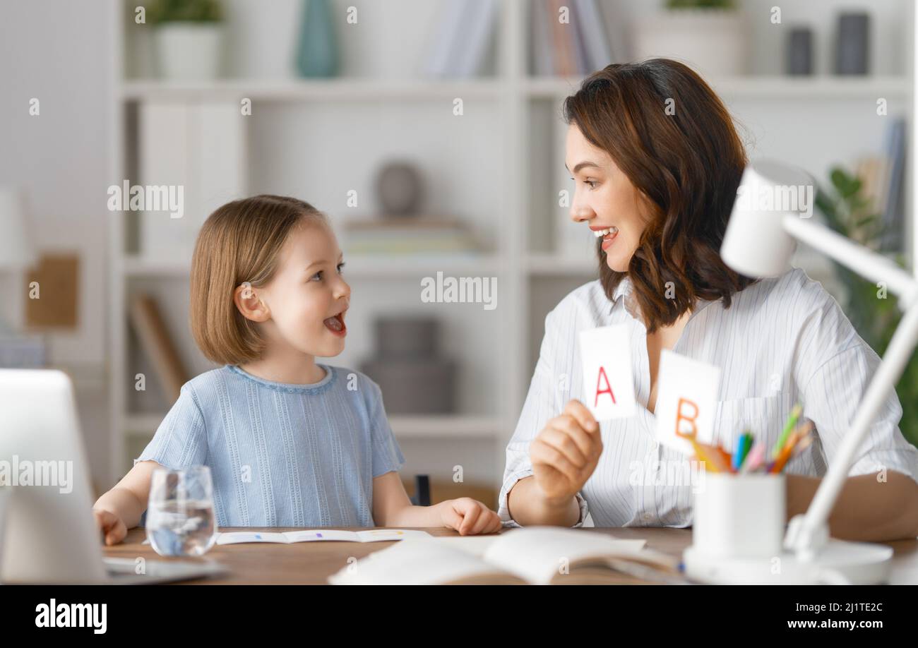 Happy child and adult are sitting at desk. Girl doing homework or ...