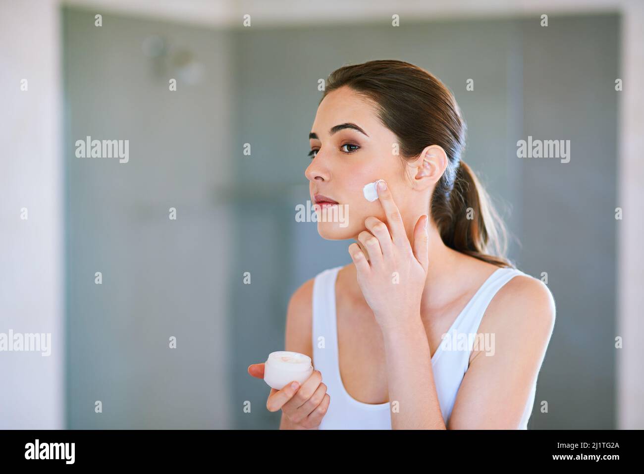 Keeping her skin clean and smooth. An attractive young woman applying ...