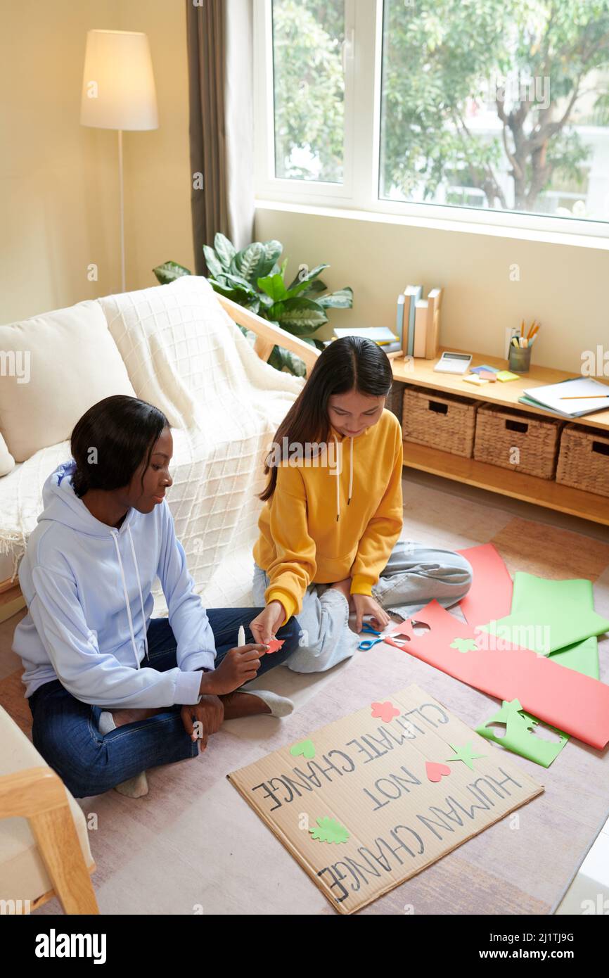 Teenage girls decorating placard they made for climate change awareness ...