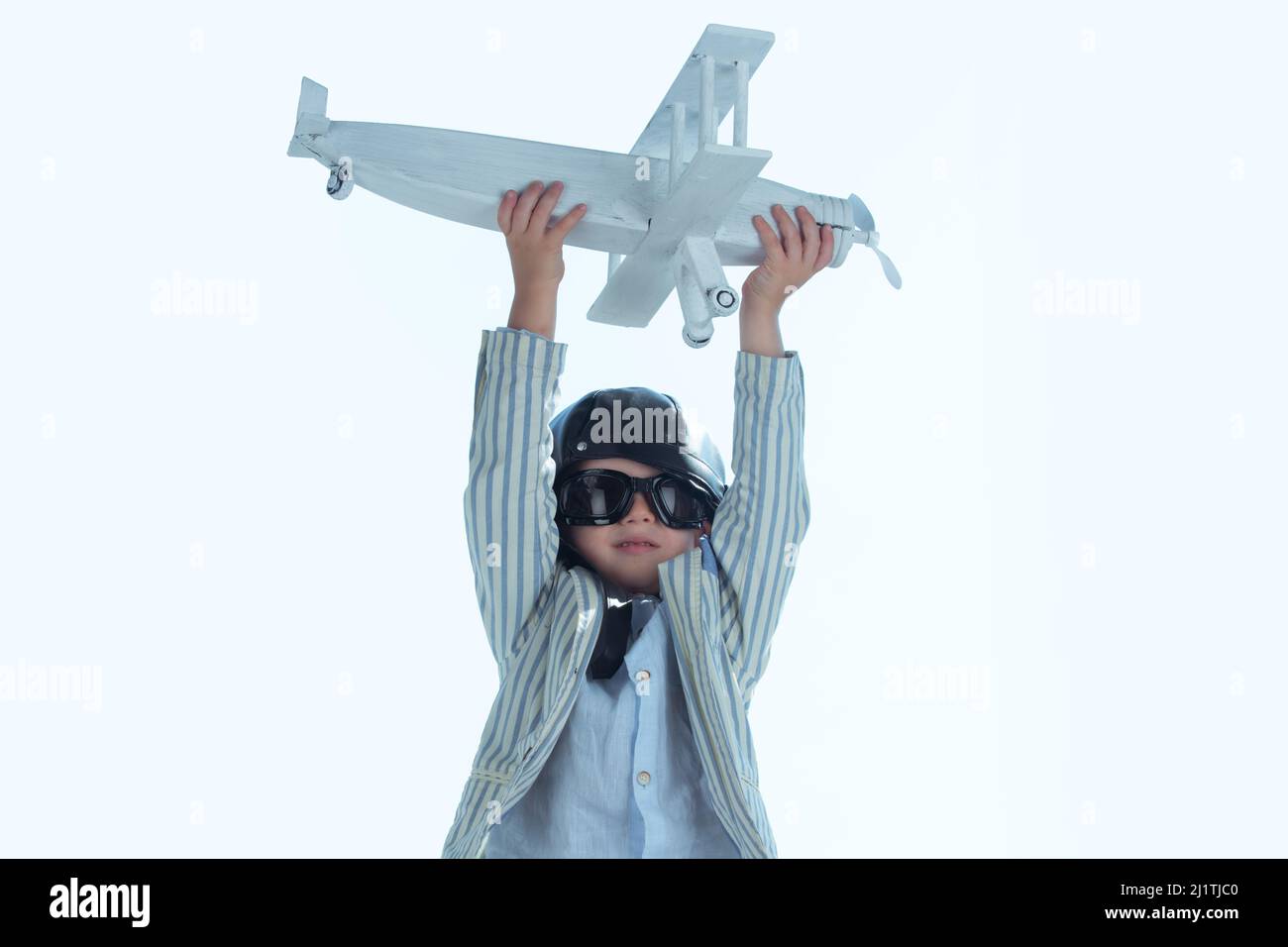 Kid with pilot goggles and helmet dreaming and plays with a toy plane ...