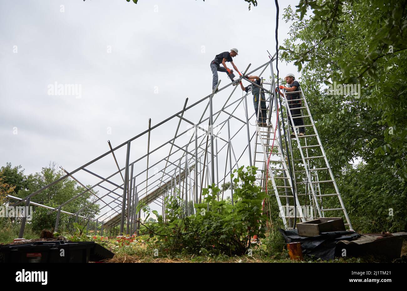 Three men in workwear installing metal poles and rails for photovoltaic ...