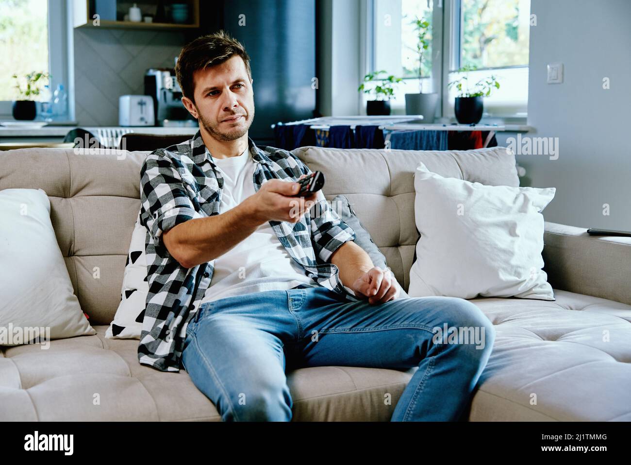 Man sitting on sofa and watching TV, switch channels using remote ...