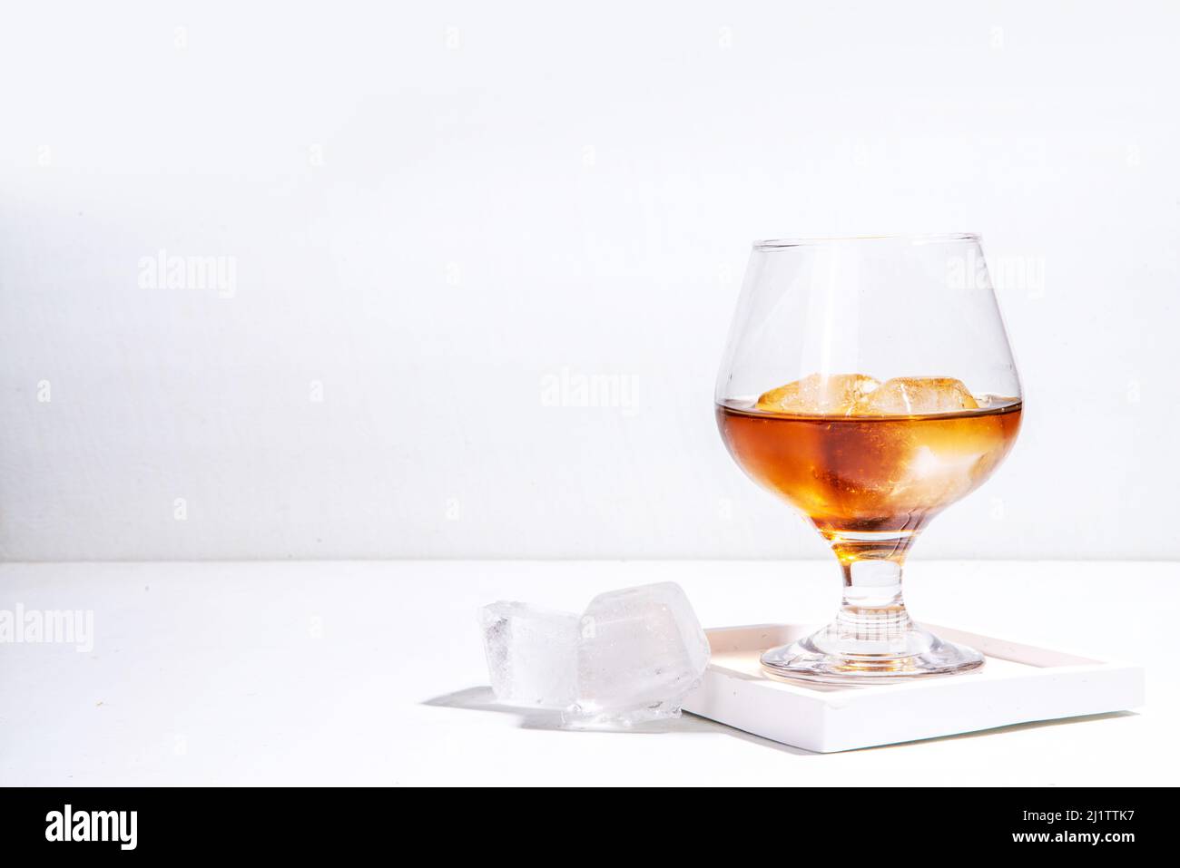 Strong alcohol drink glass. One glass of cognac or whiskey with ice cubes on white tile ...