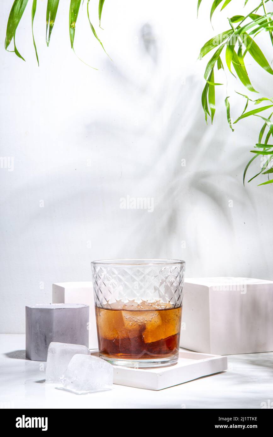 Strong alcohol drink glass. One glass of cognac or whiskey with ice cubes on white tile ...
