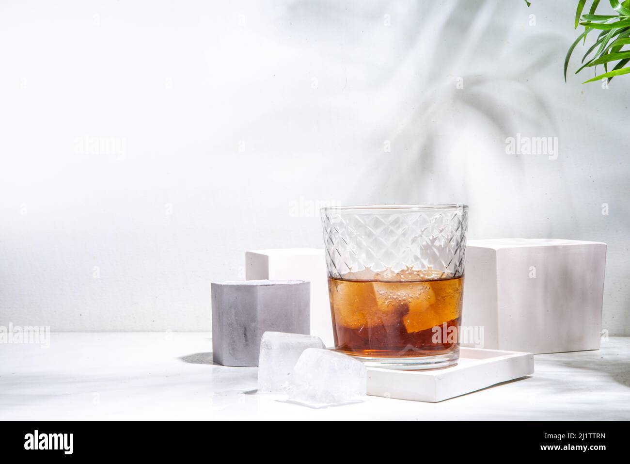 Strong alcohol drink glass. One glass of cognac or whiskey with ice cubes on white tile ...