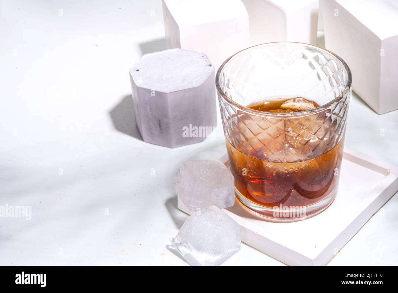 Strong alcohol drink glass. One glass of cognac or whiskey with ice cubes on white tile ...