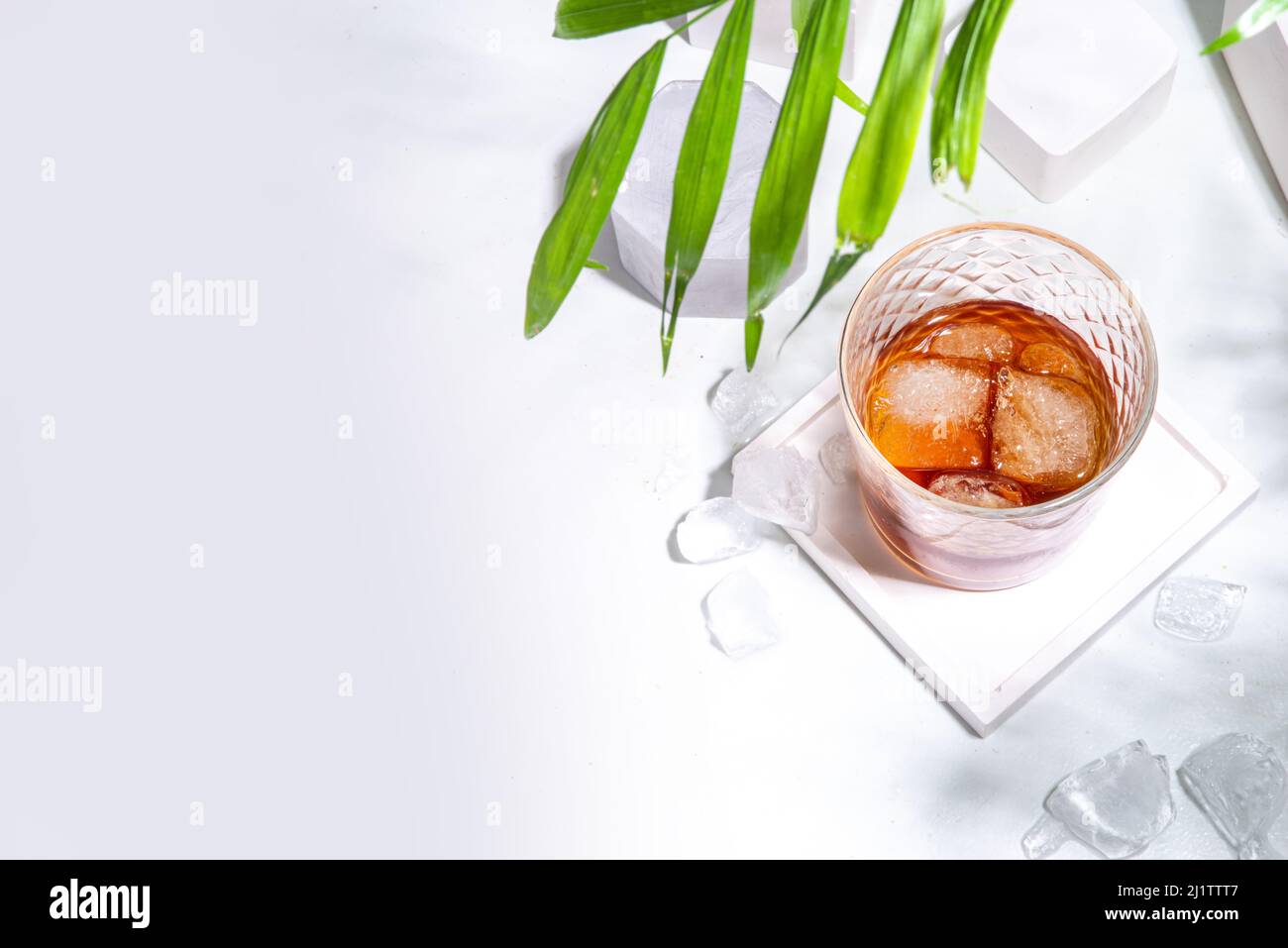 Strong alcohol drink glass. One glass of cognac or whiskey with ice cubes on white tile ...