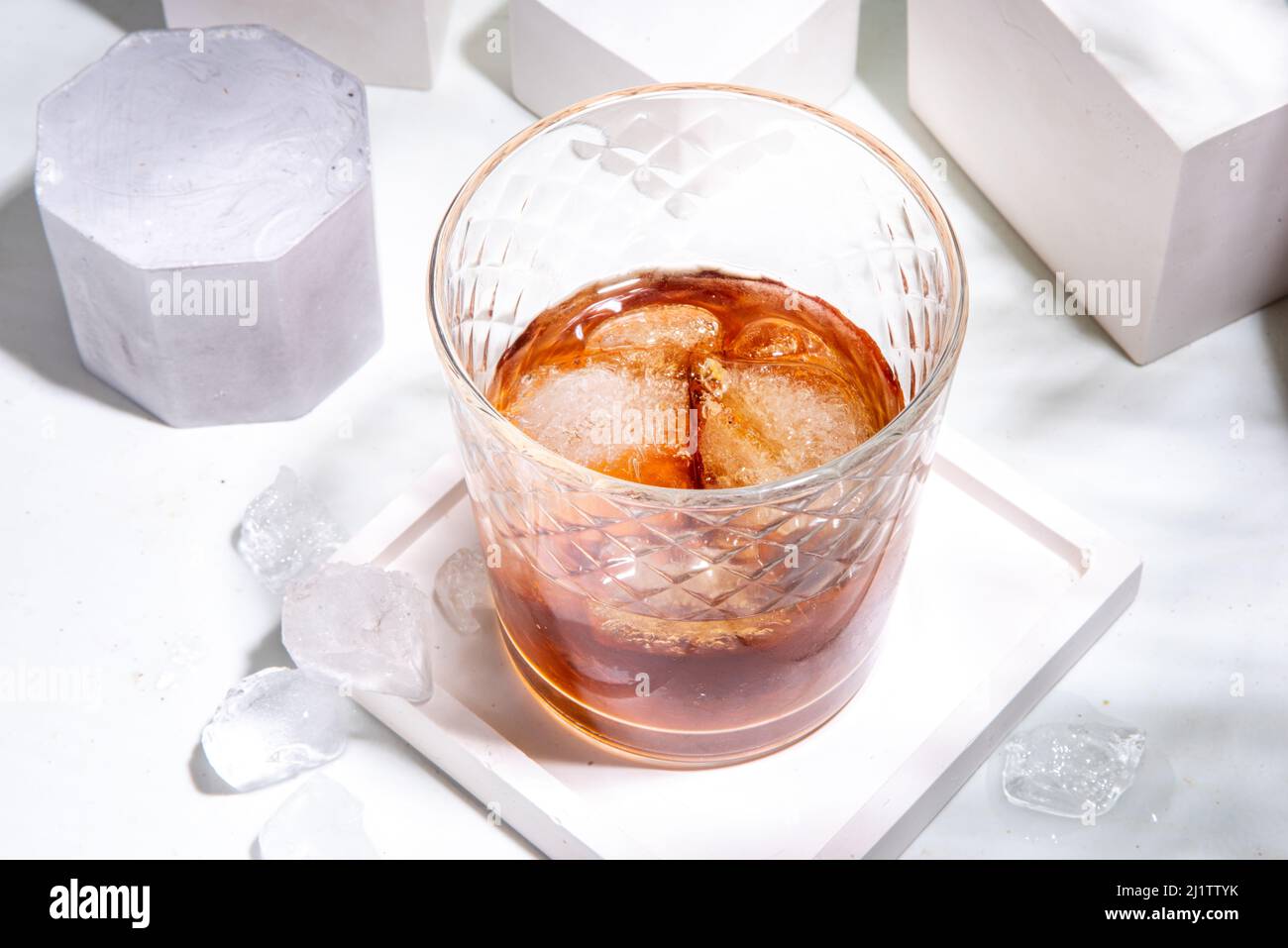 Strong alcohol drink glass. One glass of cognac or whiskey with ice cubes on white tile ...