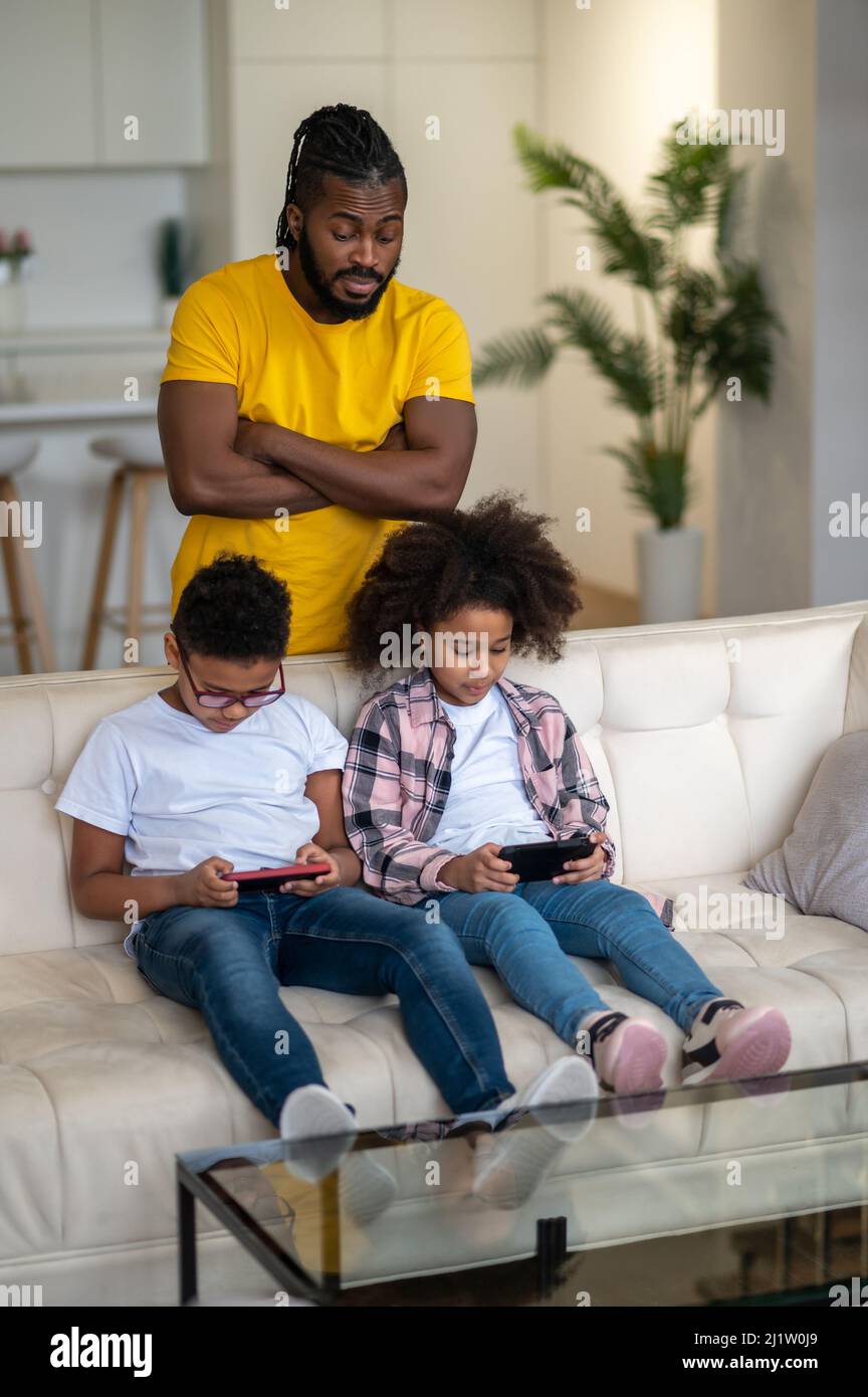 Dad watching children intently looking at smartphones Stock Photo - Alamy