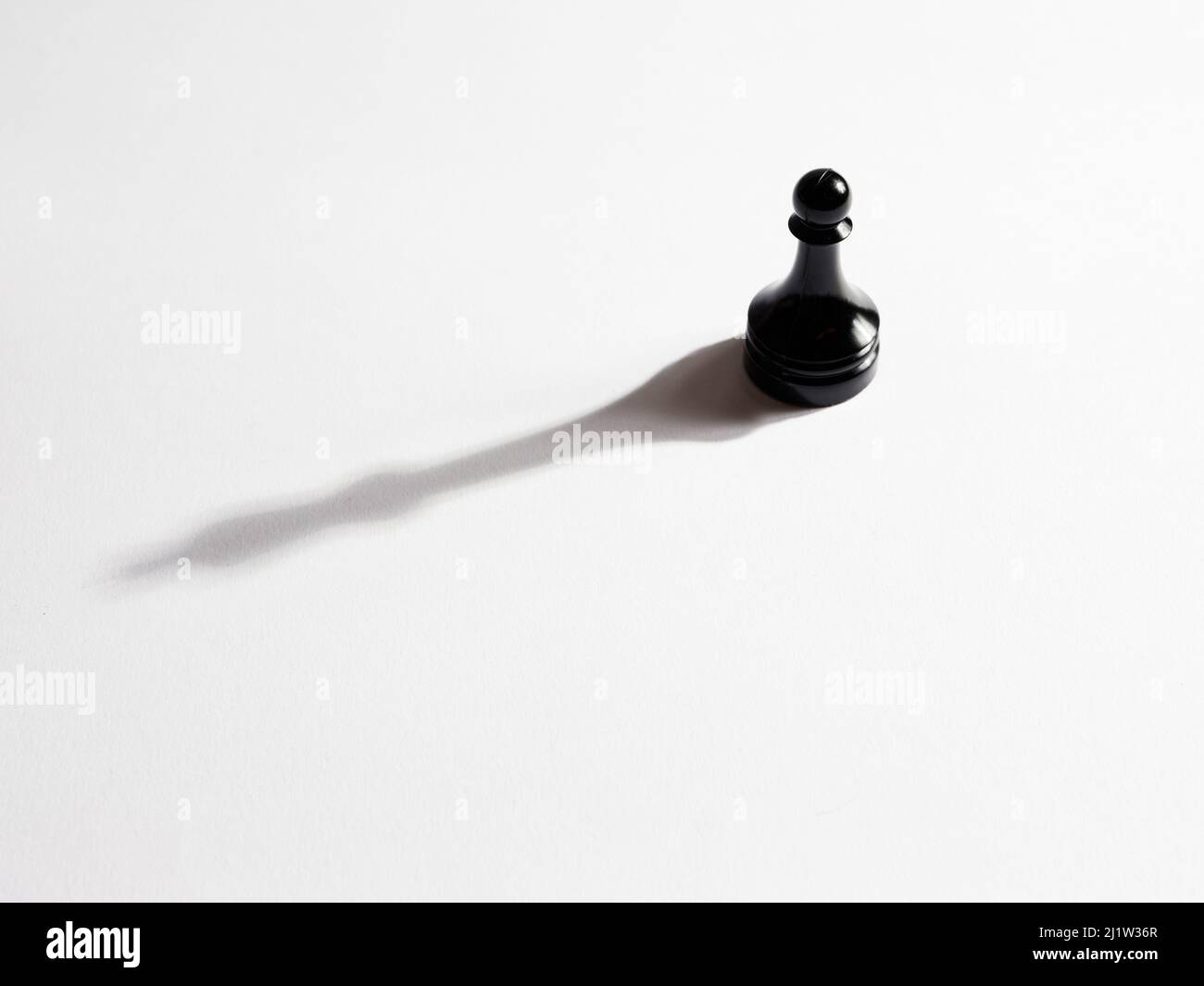 Top view of a black chess pawn with the shadow of a king on white ...